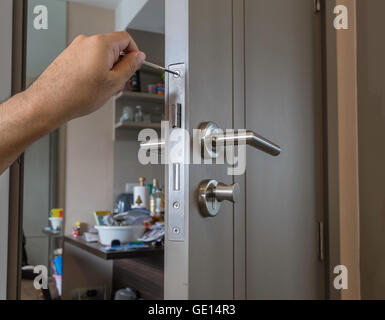 A locksmith is repairing an interior door lock. Close-up of male hands ...