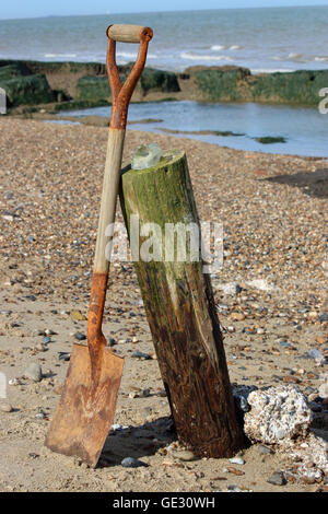 Old wooden handled spade leaning against a half buried breakwater on a ...