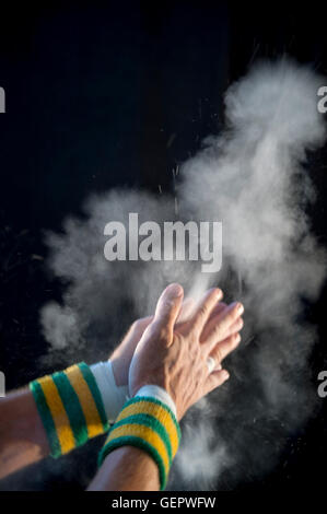 Taped hands of gymnast clapping white chalk powder into a cloud against ...