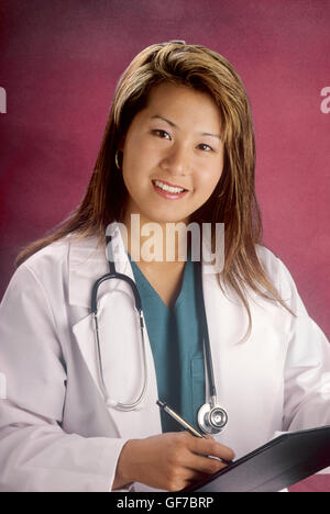 Young Asian female doctor in scrubs writing notes while using laptop ...