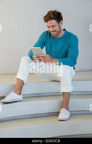 Happy young man using tablet computer while sitting on sofa at home ...