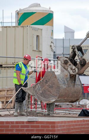 Workers place concrete blocks in row on building site surrounded by ...