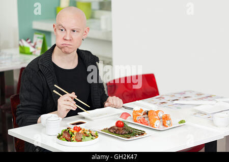 Young hispanic man eating sushi using chopsticks smiling happy pointing ...