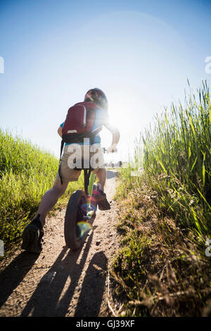 Rear view of boy wearing cycling helmet while riding bicycle on road ...