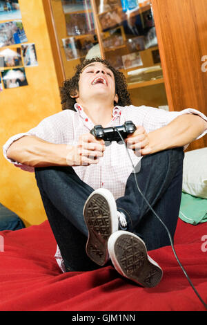 Hispanic teenager playing video game holding controller pointing finger ...
