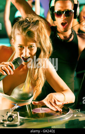 Two DJs - male and female, black and white - in a club at the turntable ...