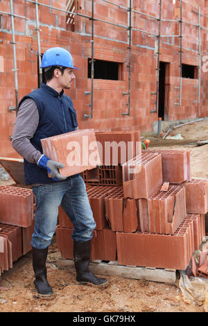 Hard working bricklayer lays bricks on cement mix on construction site ...