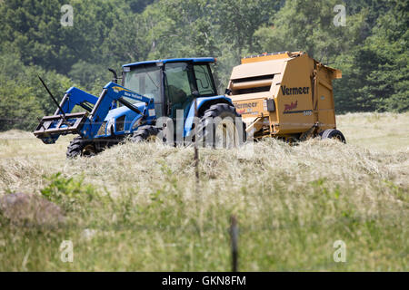 A tractor pulling a baling machine is at work producing square bales in ...