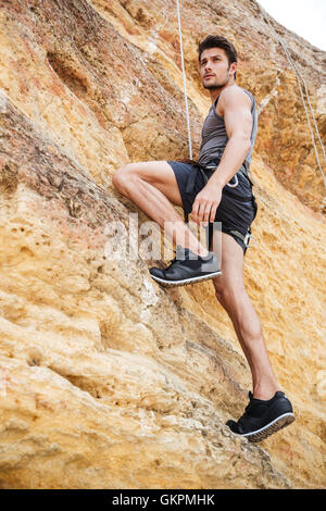 Young man climbing steep wall of rocky mountain. Male climber overcomes ...