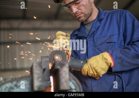 Mechanic wearing safety goggles using drilling machine in workshop ...