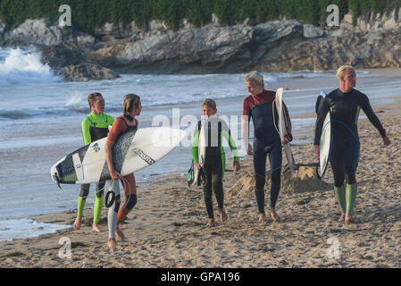 Group of happy surfers in wetsuits running into the sea holding ...