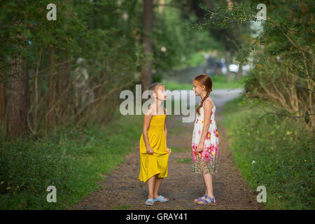 Two little sisters standing talking near a tree in the Park Stock Photo ...