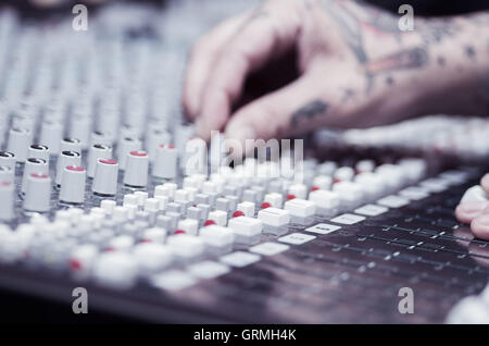 Closeup of hands covered with tattoos working on mixer console ...