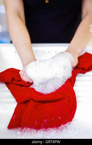 Closeup womans hands handwashing clothes in red plastic washbucket ...