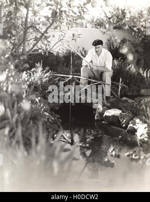Fishing in the 1940s. A man is sitting by the lake fishing with a rod ...