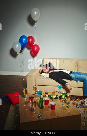 Drunk young man with champagne sleeping on sofa after New Year party at ...