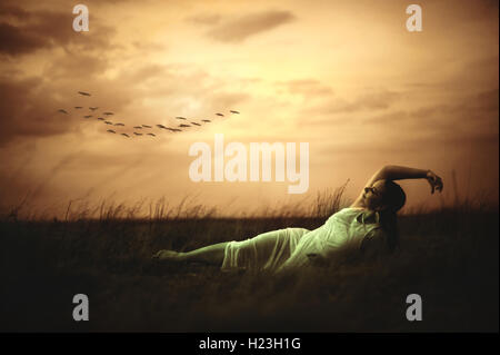 A woman lying in a field of grass with her legs raised against the ...