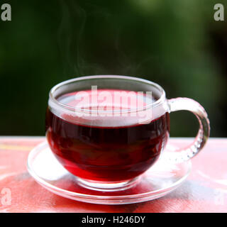 Red Hot Hibiscus tea in a glass mug on a wooden table among rose petals ...