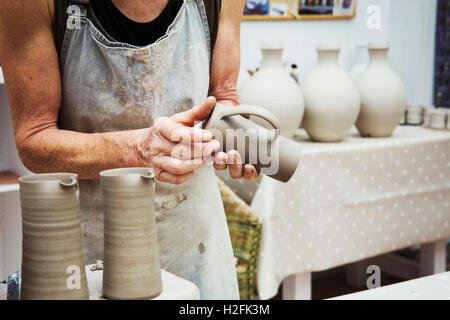 A potter handling a wet clay pot, smoothing clay and preparing it for ...