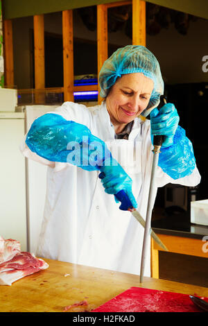 Woman working in a butchery, wearing protective clothes and gloves ...