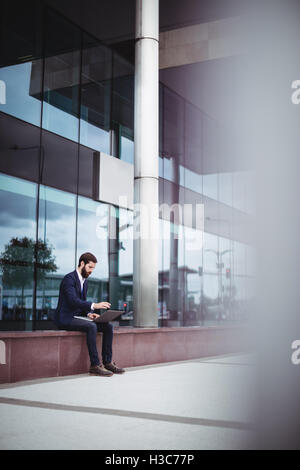 Businessman sitting by pillar, using laptop Stock Photo - Alamy