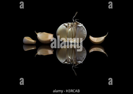 One halved and three peeled garlic isolated on a black reflective ...