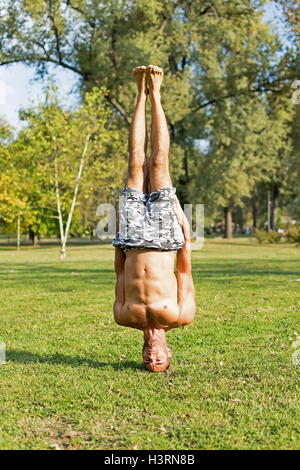 Male yoga standing on his head and hands, meditation, grey background ...