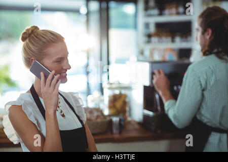 Young waitress talking on smartphone while waiter preparing food in ...