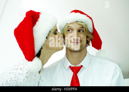 Young couple in Santa hats and pajamas kissing on beige background ...