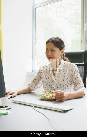 businesswoman looking having food while using laptop computer at desk ...