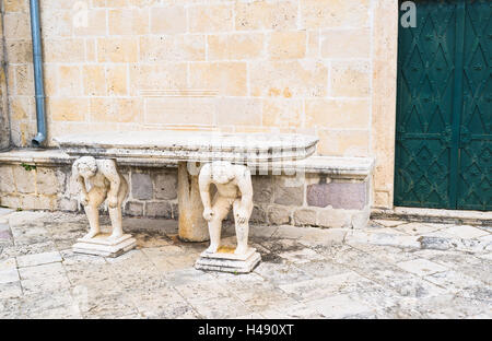A medieval stone table is supported by two statues of the hunched men ...