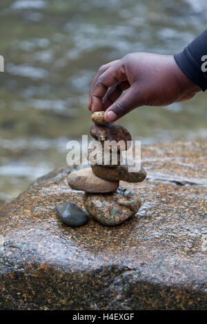 Hand placing a stone on a rock surface with small pebbles in an outdoor ...