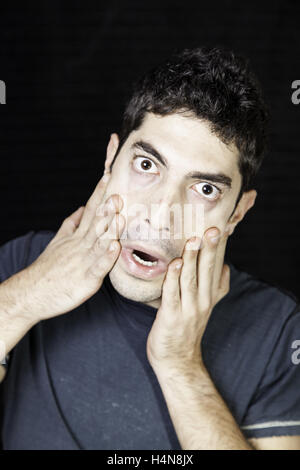 Frightened young guy with eyes wide open wearing pajamas eating popcorn ...