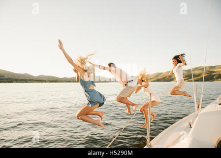 Four people jumping off the side of a sail boat into a lake Stock Photo ...