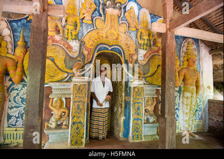 Care taker at the entrance to an ancient cave temple, Raswehera forest ...