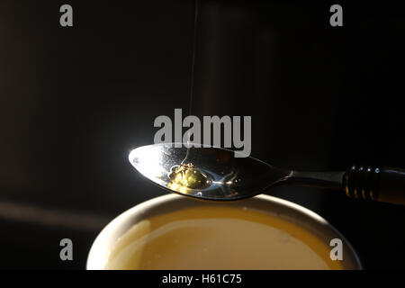 Teaspoon filled with honey poured into cup of tea Stock Photo - Alamy