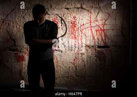 Man holding a sickle standing near blood stained wall for concept about ...