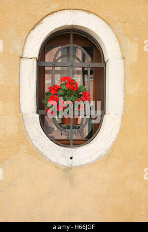 Bright red stone oval window frame in a white wall with black metal ...