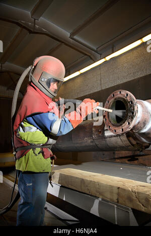 A worker uses high-pressure grit blasting to clean petrochemical pipes ...