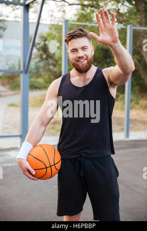 Portrait of friendly smiling man waving raised hand, saying hello and ...