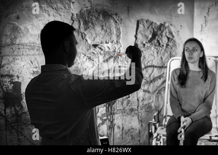 Shadowy male figure pours liquid from beakers in front of afraid female ...