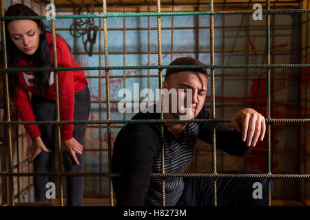 Victims imprisoned in a metal cage with a blood splattered wall behind ...