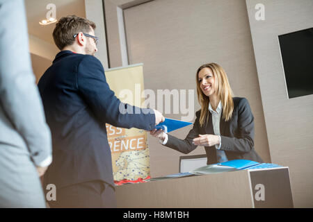 Receptionist giving file to businessman at convention center Stock ...