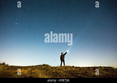 Caucasian man pointing flashlight at night sky near water Stock Photo ...
