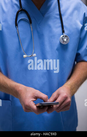Man in surgeon uniform browsing modern smartphone while leaning on wall ...