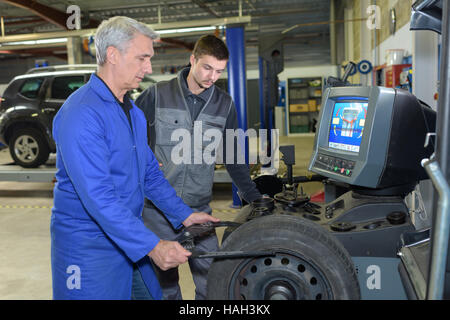 apprentice mechanic and teacher retreading wheel in automotive workshop ...
