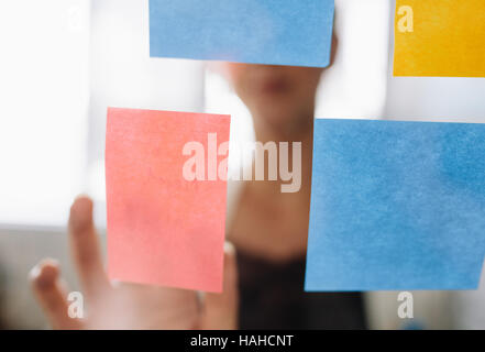 hand pointing at adhesive notes on glass wall at workplace. Sticky note ...