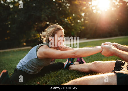 Holding hands couple stretching on garden lawn, man T-shirt, woman pink ...