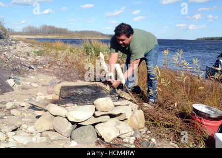 An indigenous man making bannock on a stick, a native North American ...