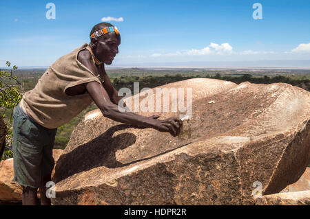 Hadzabe tribesman pounding on a resonant rock to communicate over a ...